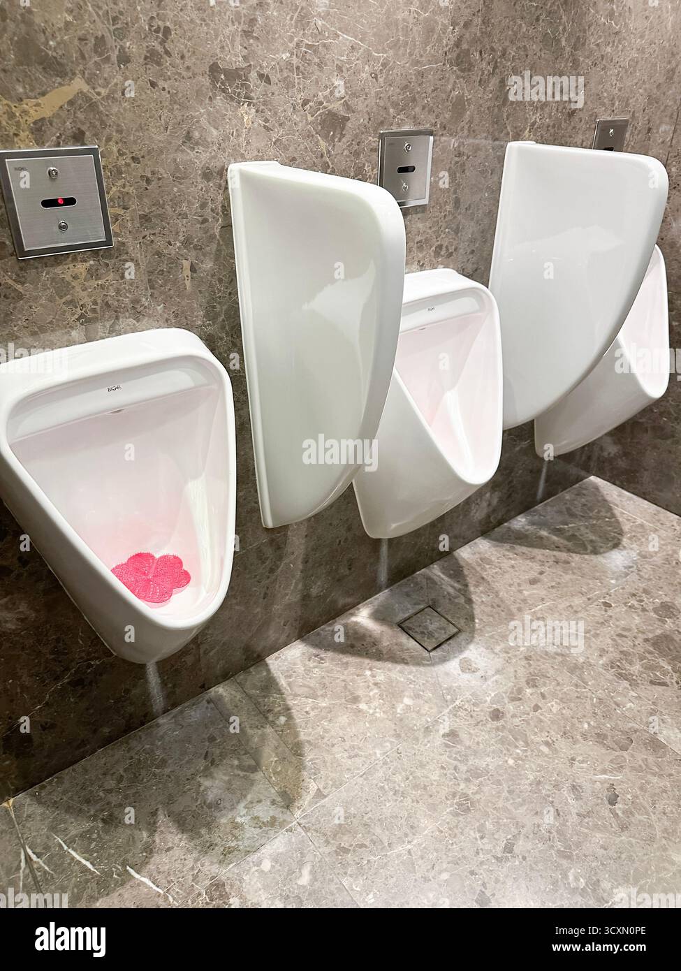 Three white porcelain urinals with a pink urinal cake on a marble tiled ...
