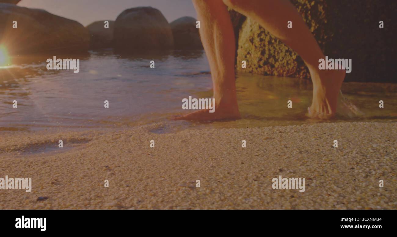 Stepping barefoot man wearing trunks into shallow water on beach ...