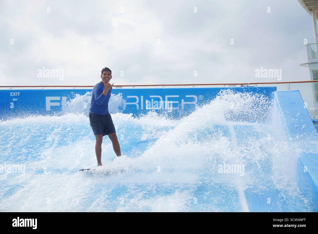 Smiling guest gestures while surfing on the FlowRider simulator aboard ...
