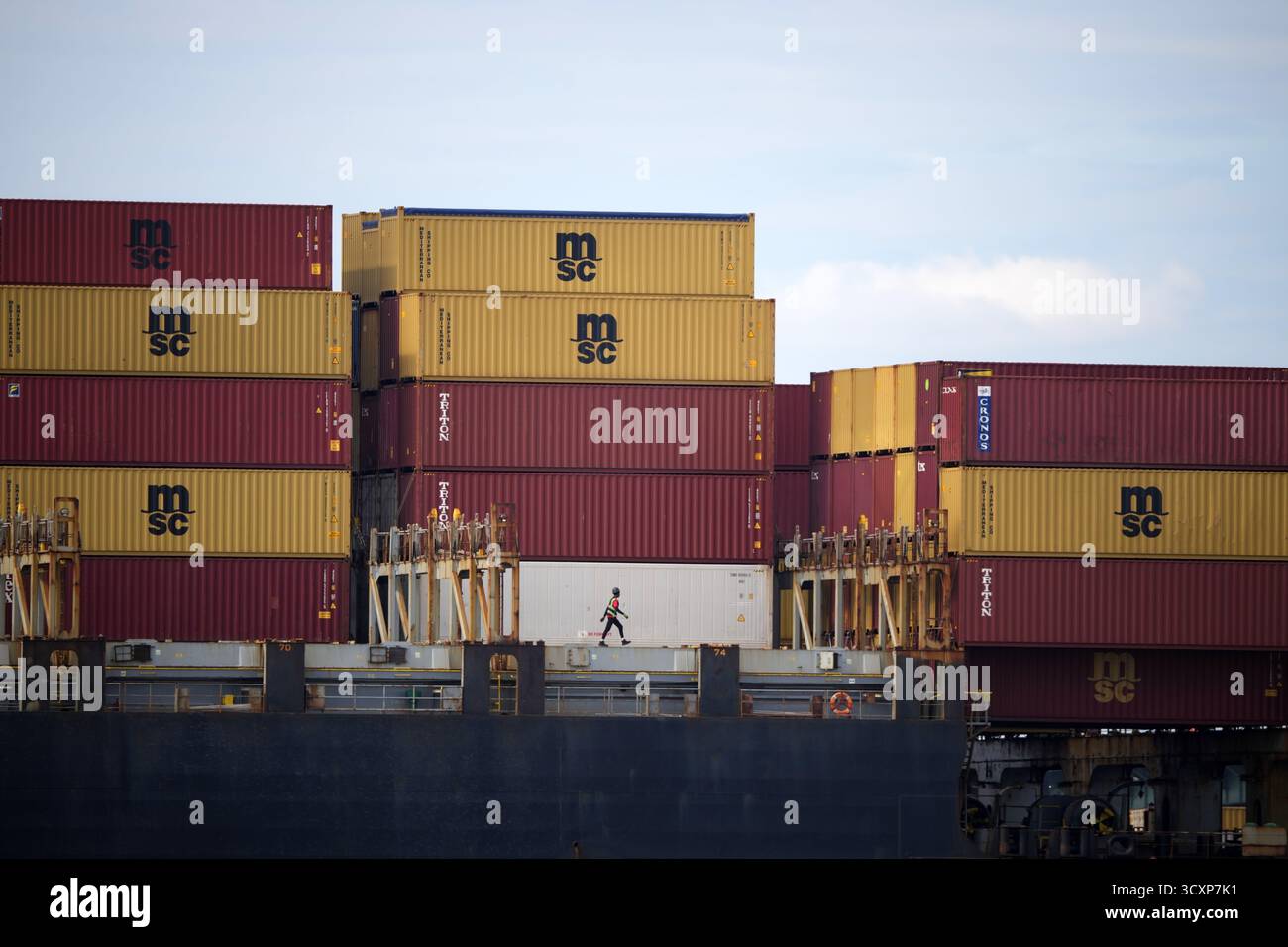 A worker walks across a ship loaded with containers at the Port of ...