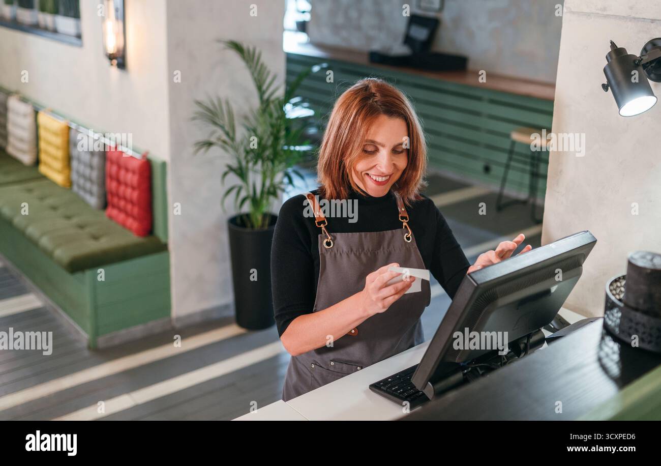 Smiling waitress in black uniform using point-of-sale terminal to ...