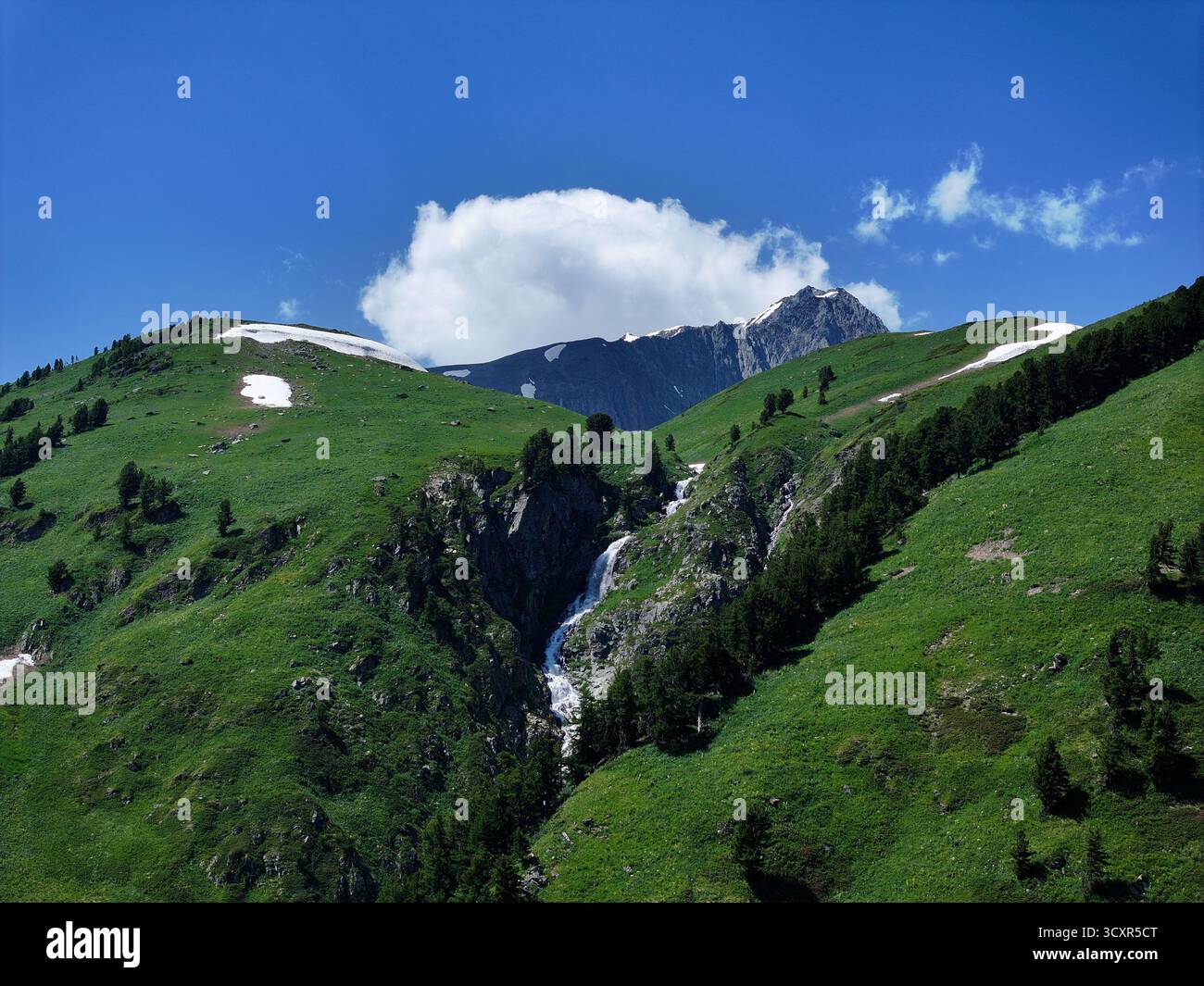 Lush green alpine meadow and steep mountainside featuring a waterfall ...
