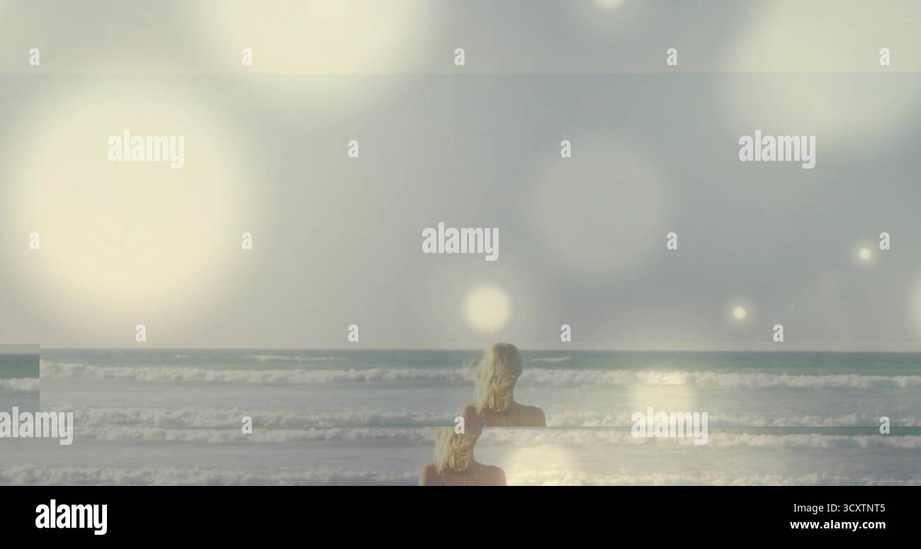 Standing mid-adult woman wearing dark swimsuit facing ocean at sandy ...