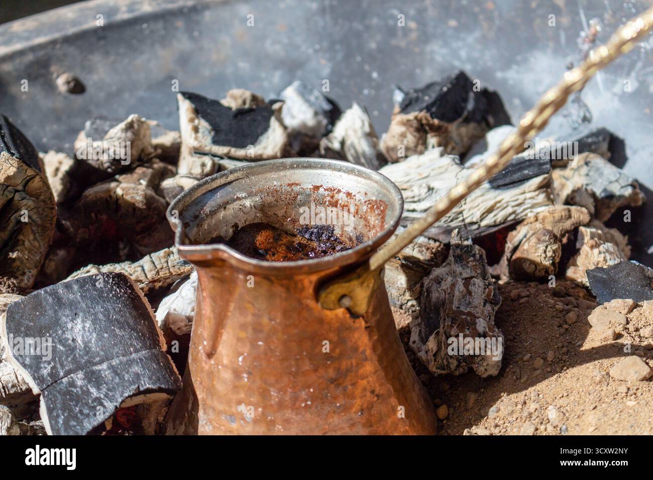 Traditional arabic coffee brewing on hot embers in a copper cezve ...