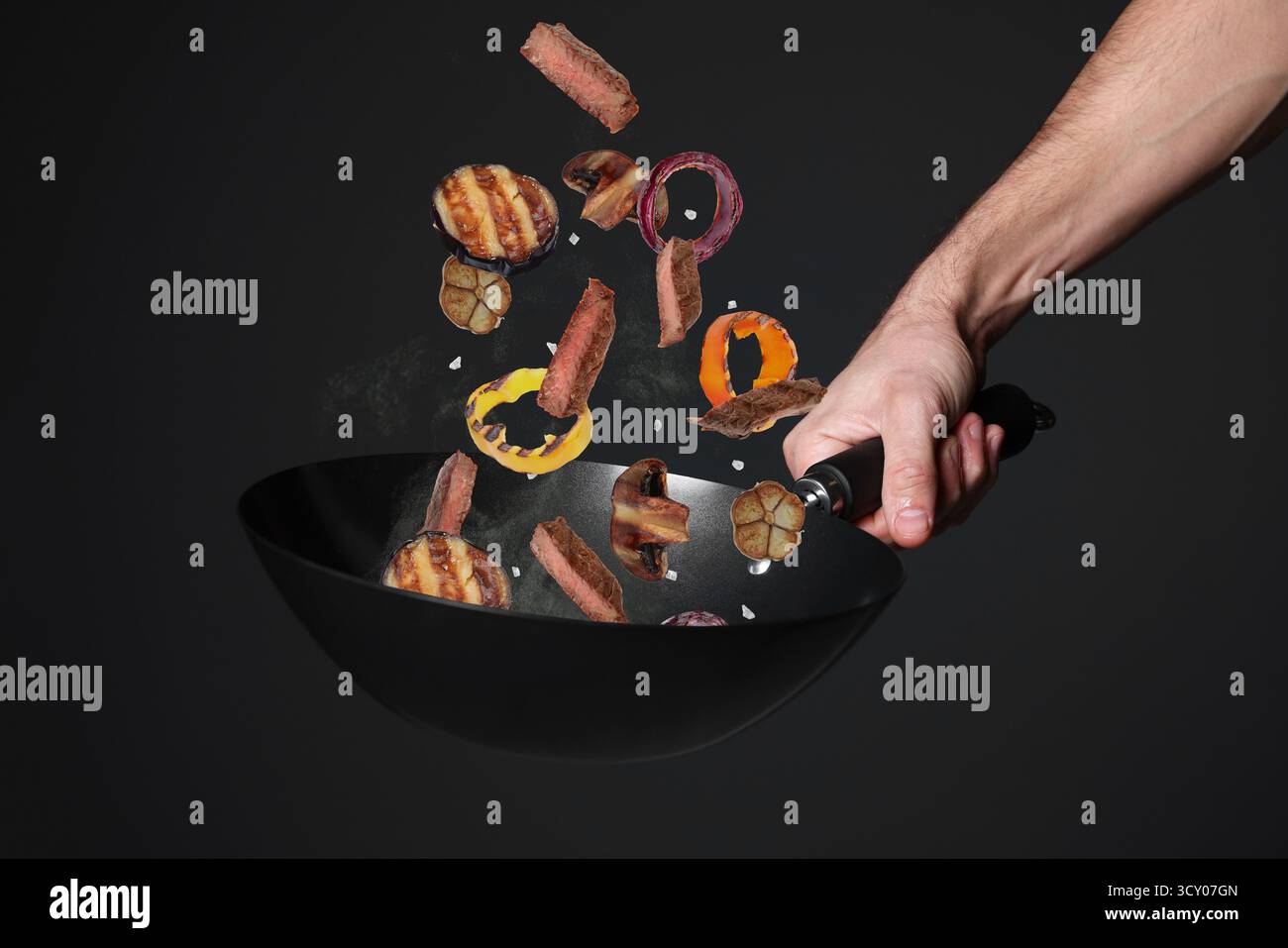 Chef tossing meat and vegetables pieces in cooking pan against black ...