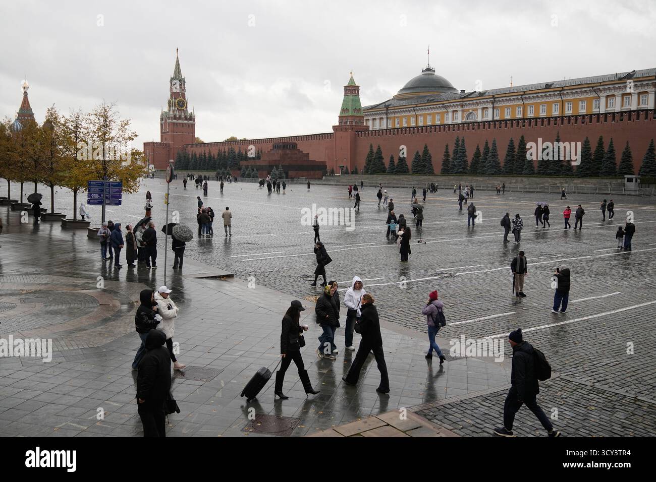 People walk under the rain through Red Square with the Spasskaya Tower ...