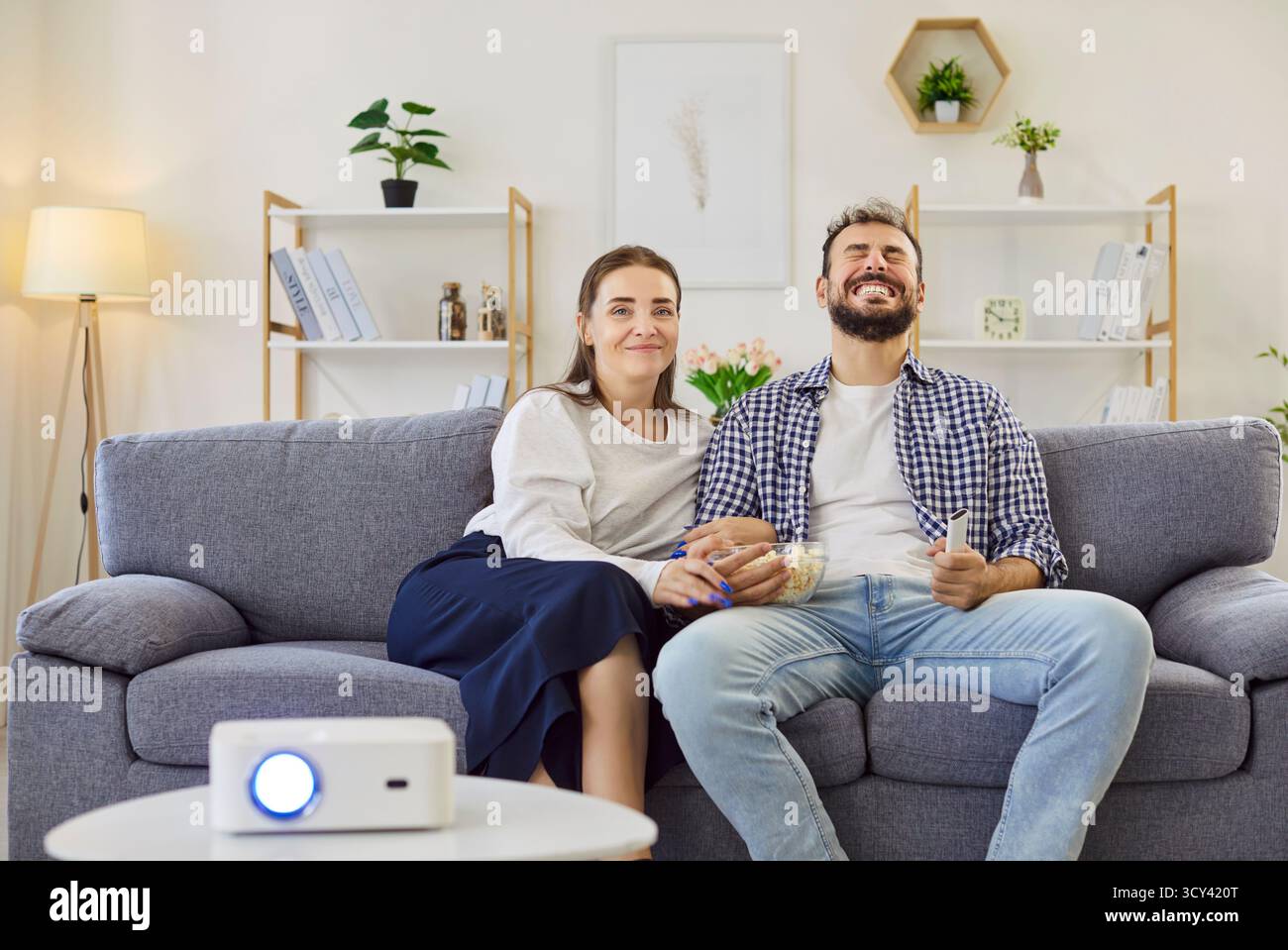 Happy couple watching TV movie with laughter, using projector at home ...