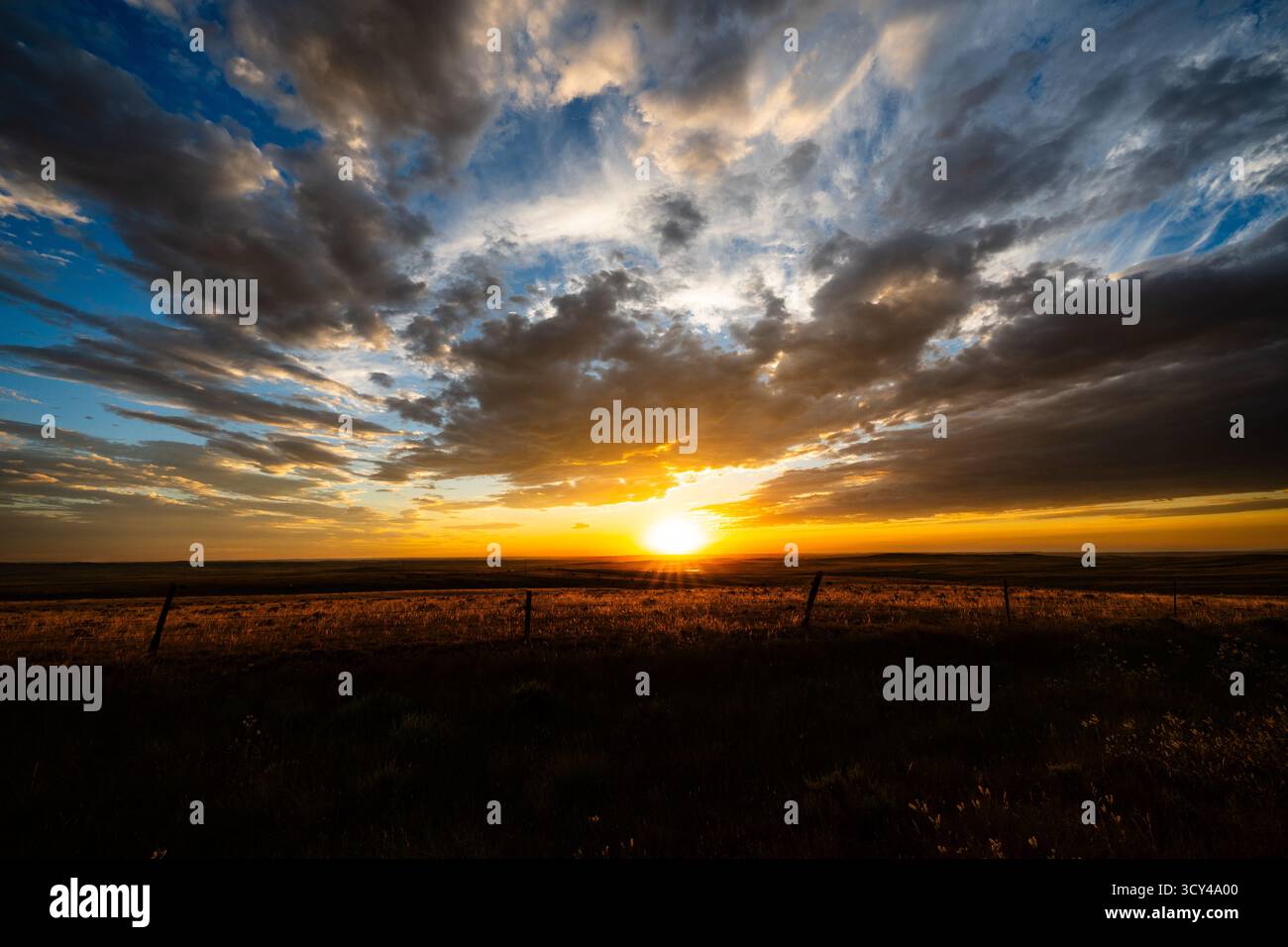 Setting sun rays shine through peaceful summer clouds over fields, creating a moody sky with ...