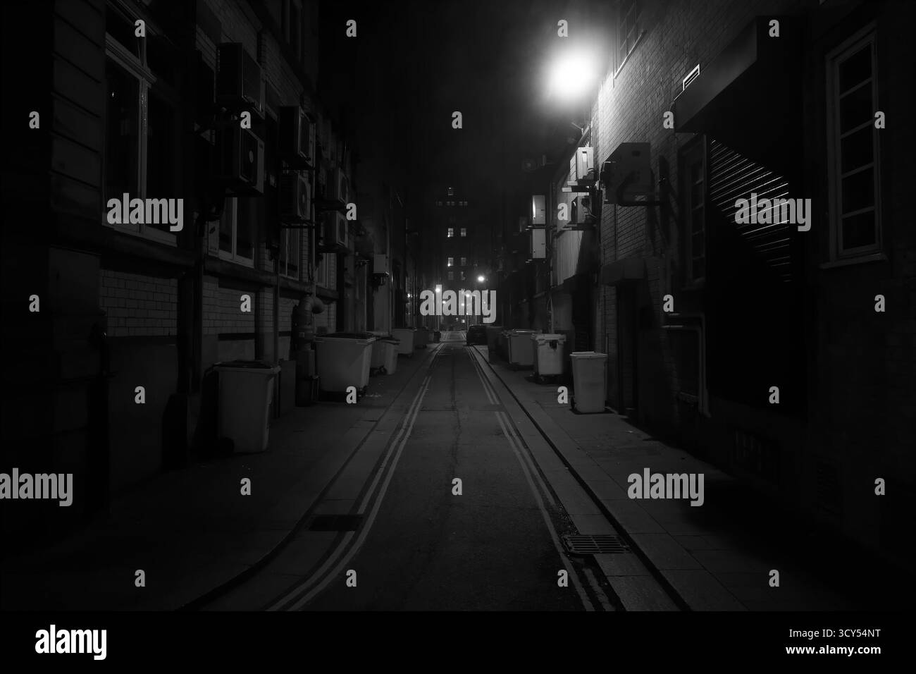 Moody black and white night scene of a narrow urban back alley lined ...