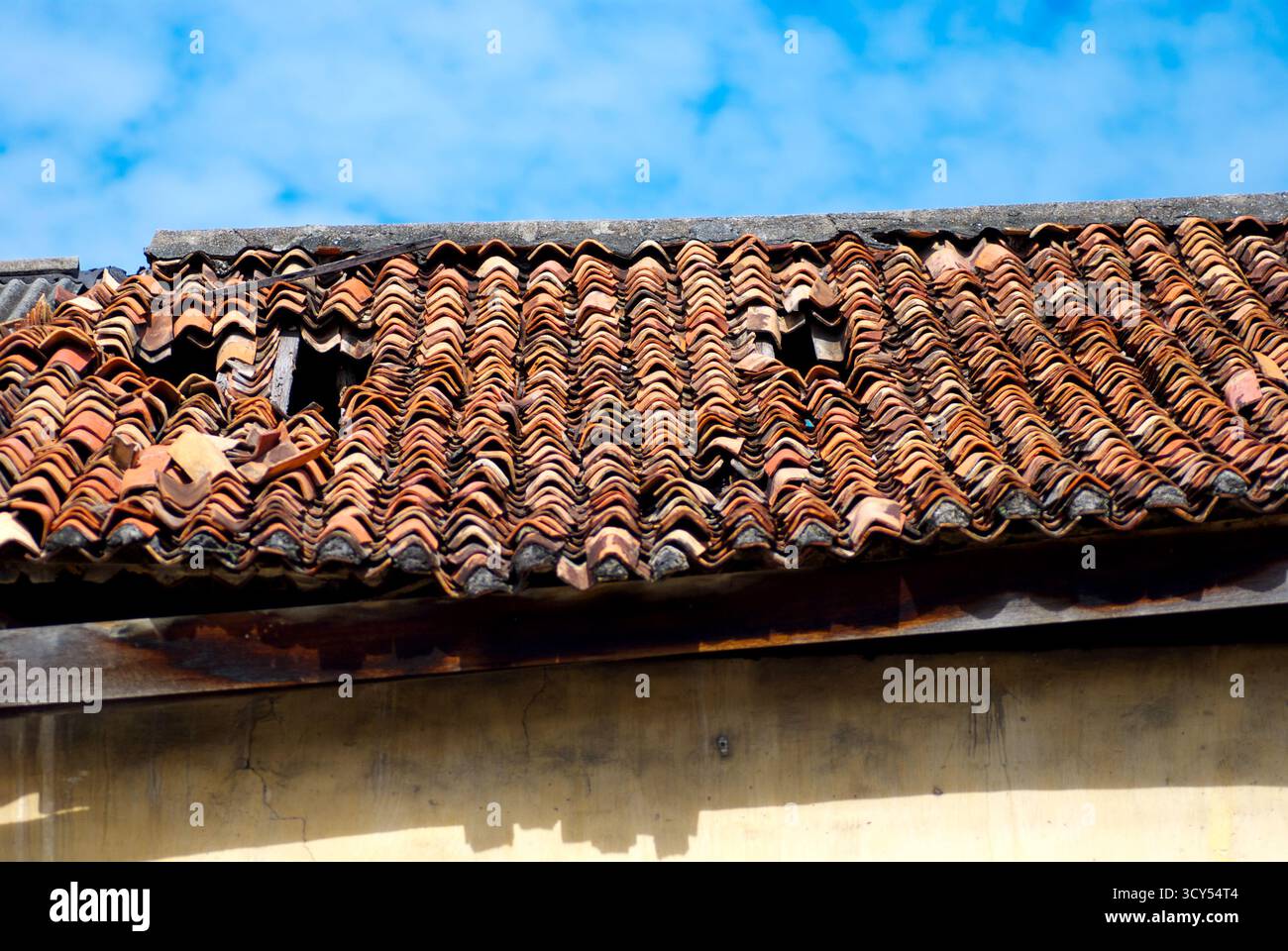 Old clay tile roof with several broken and misaligned tiles. The ...