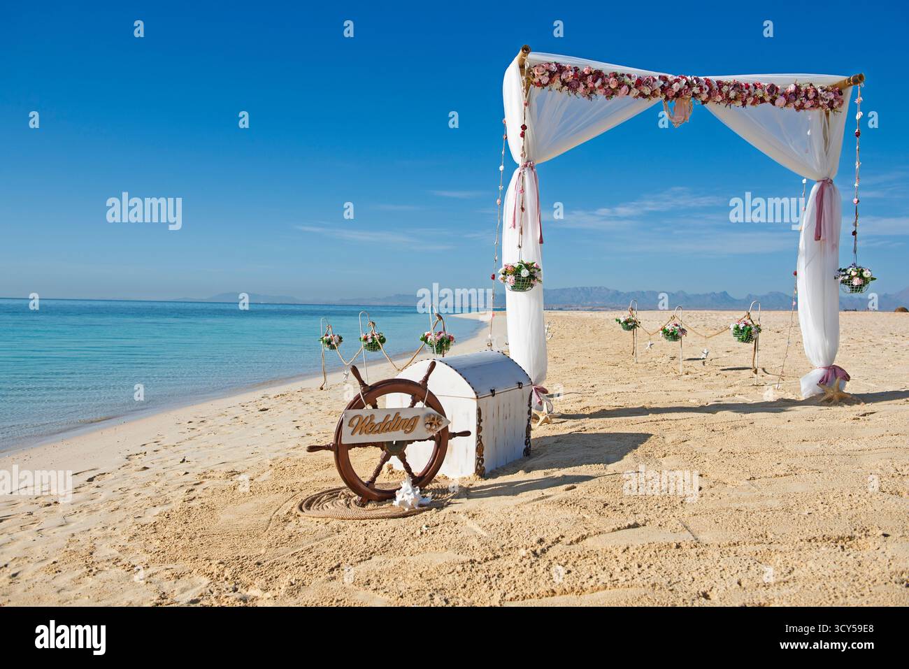 Setup of wedding day marriage aisle with drapes and arch on sandy ...