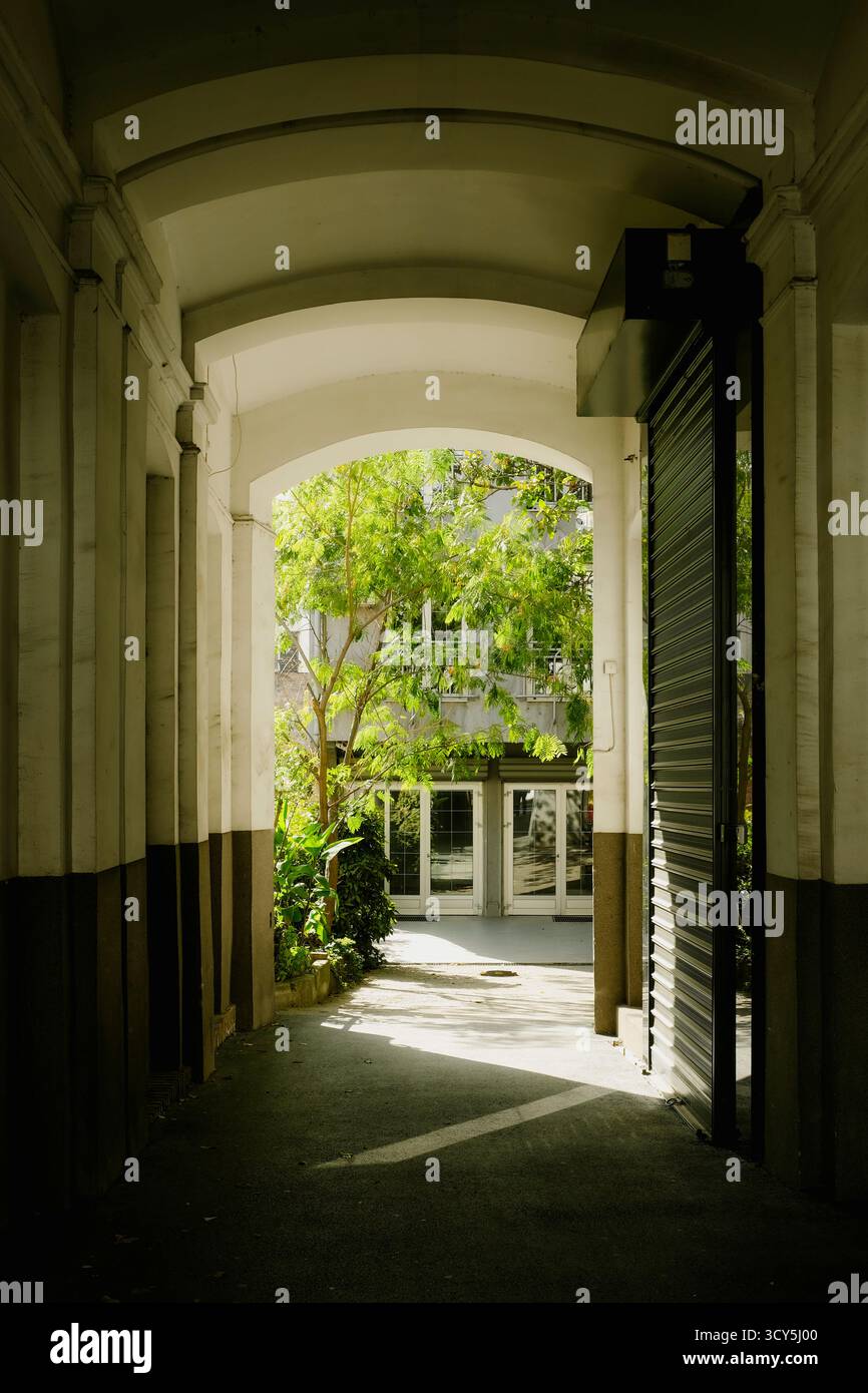 Sunlit passageway with arched ceiling leading to a courtyard filled ...