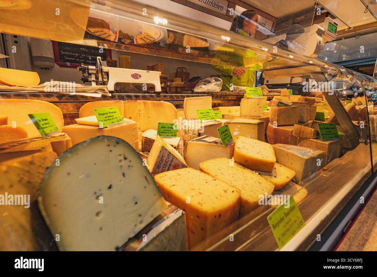 A cheese vendor in a market stall arranging various types of cheese on ...