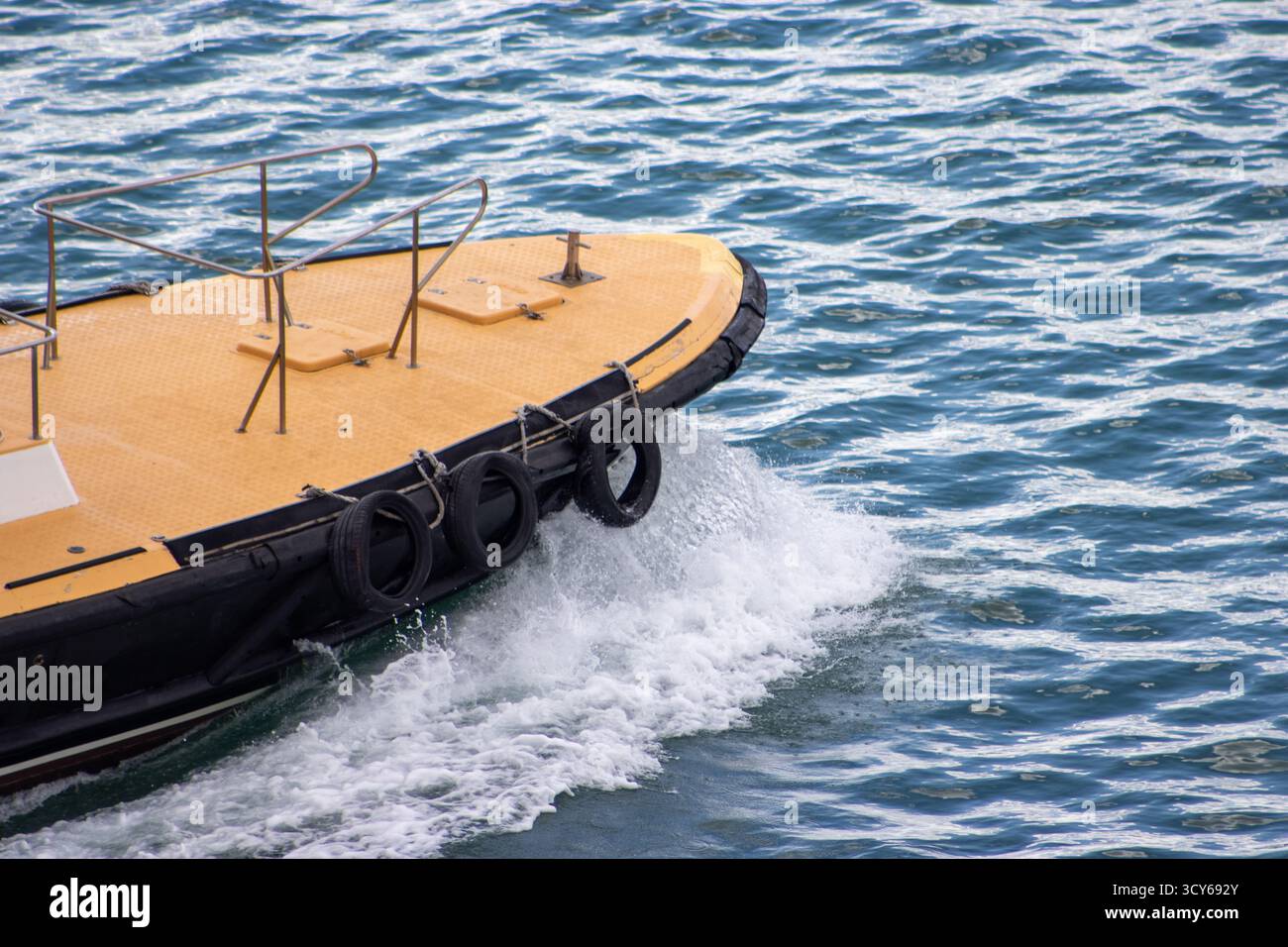 prow of a yellow and black boat running fast and making waves in a blue ...