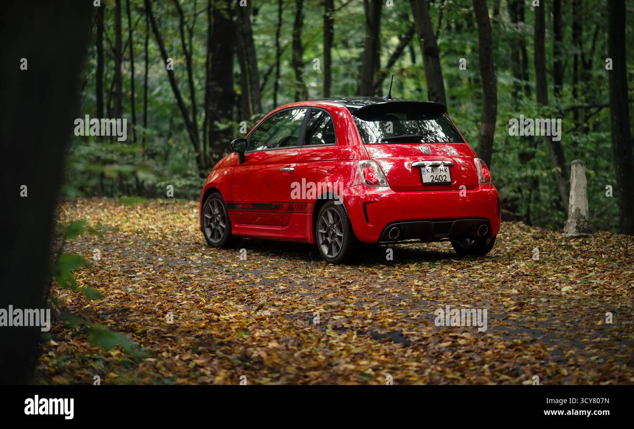 red Abarth 500 in green forest. Three quarter rear view of small sporty ...