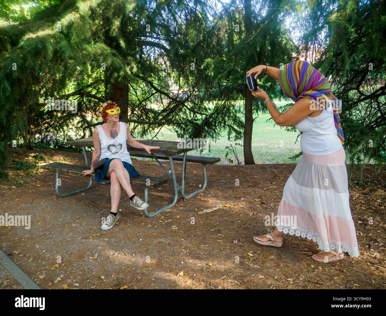 Two women enjoying a fun outdoor photoshoot in a park with masks and ...
