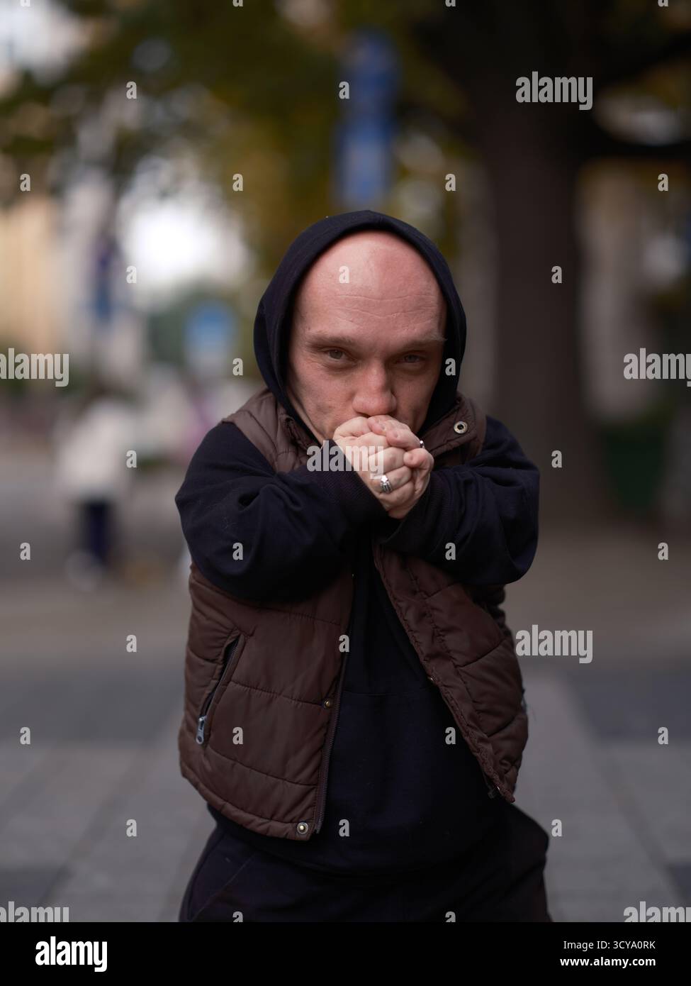 Serious man with dwarfism standing on city street, hands covering lower ...