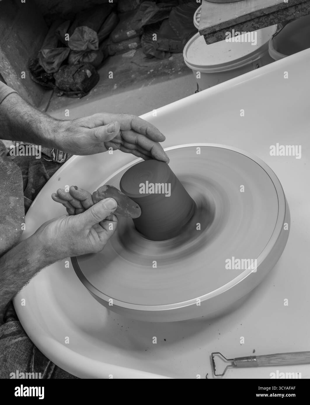 Potter at his wheel turning and finishing a clay cup or small mug Stock ...