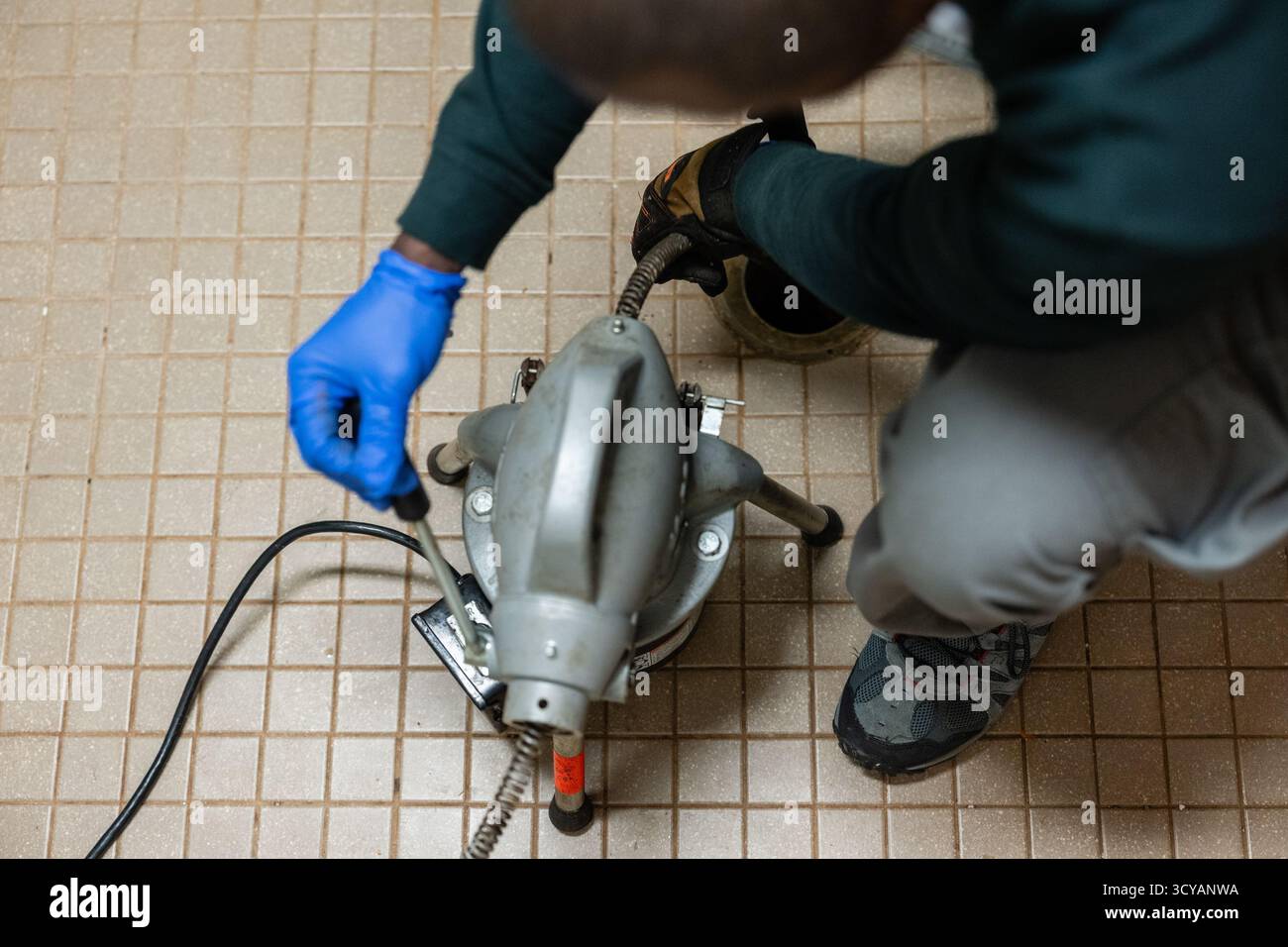 Maintenance worker Eric Frimpong, originally from Ghana, snakes a drain ...