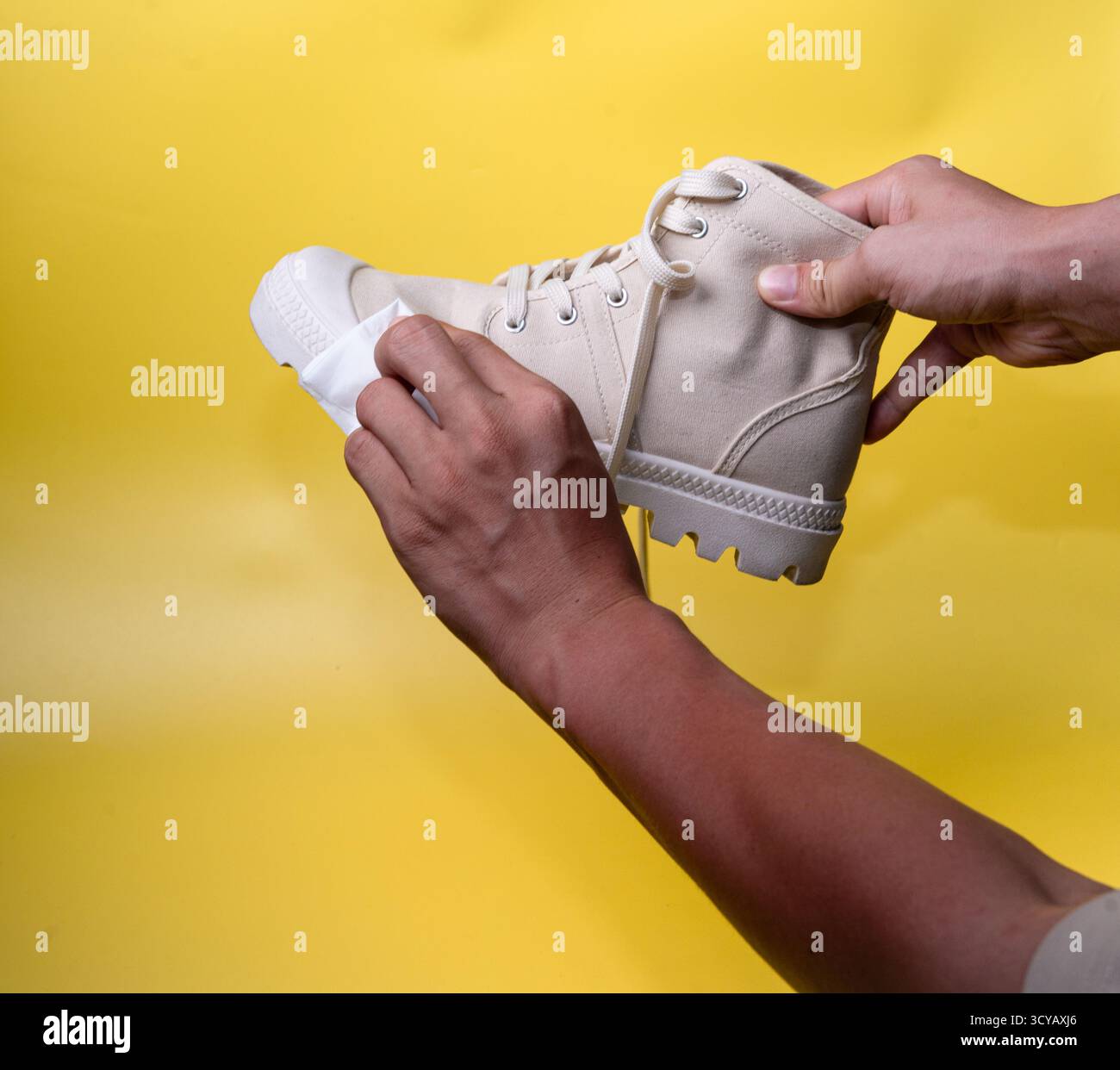 beige canvas boot being cleaned by hands against bright yellow ...