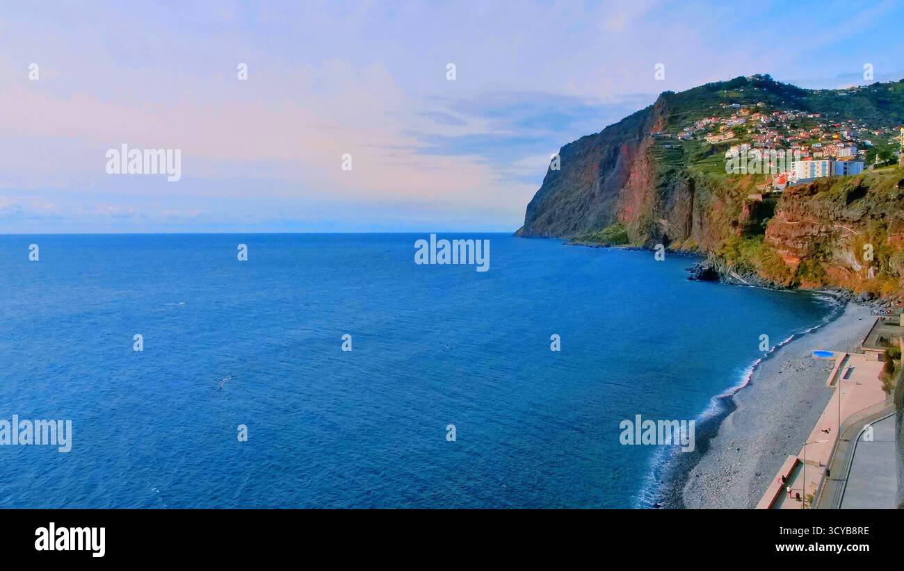 Madeira coastal cliff at sunset with ocean view, hillside houses, and ...