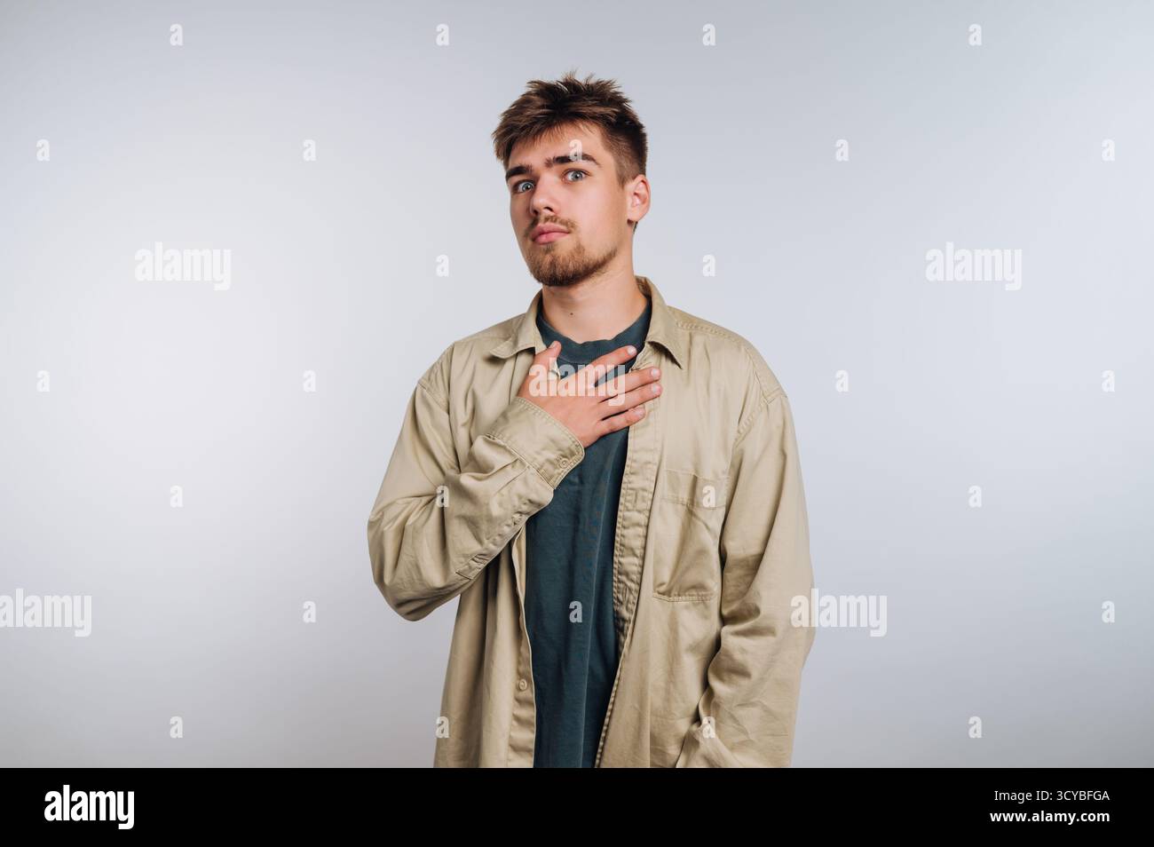 A young man stands in a neutral studio with a focused expression ...