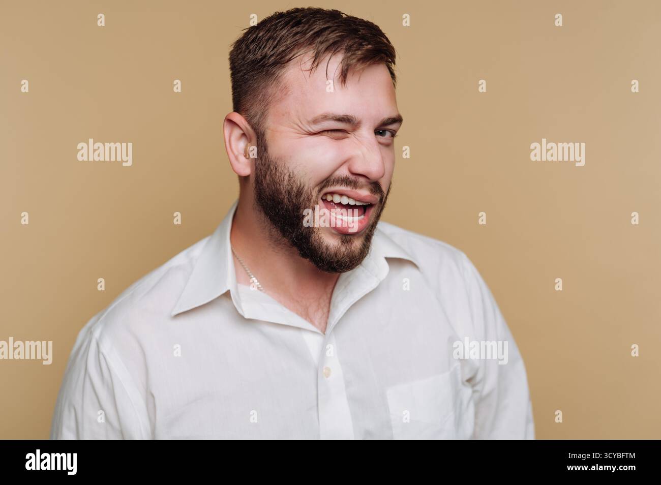 A man with a beard is winking and smiling, showcasing a playful ...