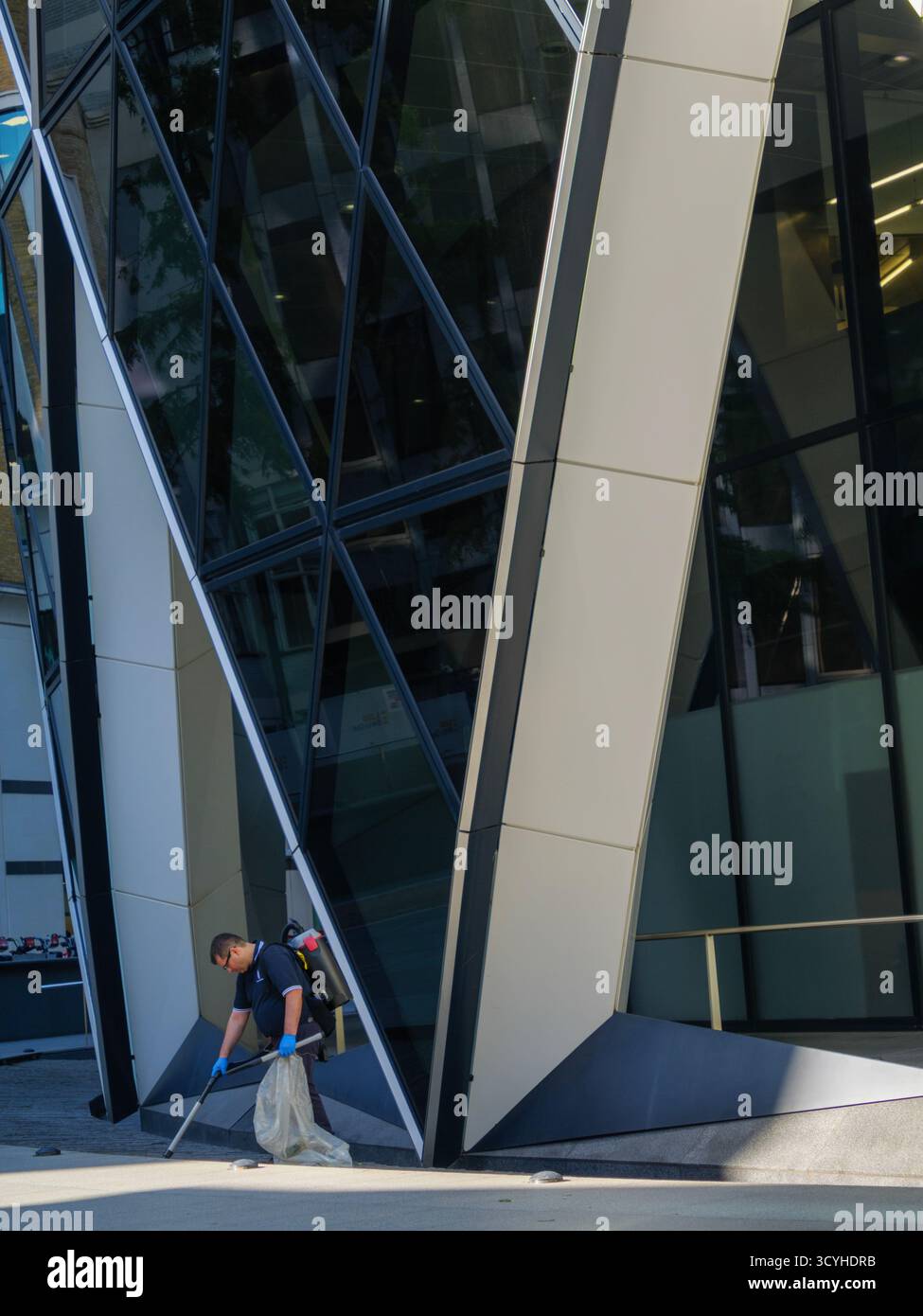 Male cleaner picking up litter at the bottom of 30 St Mary Axe also ...