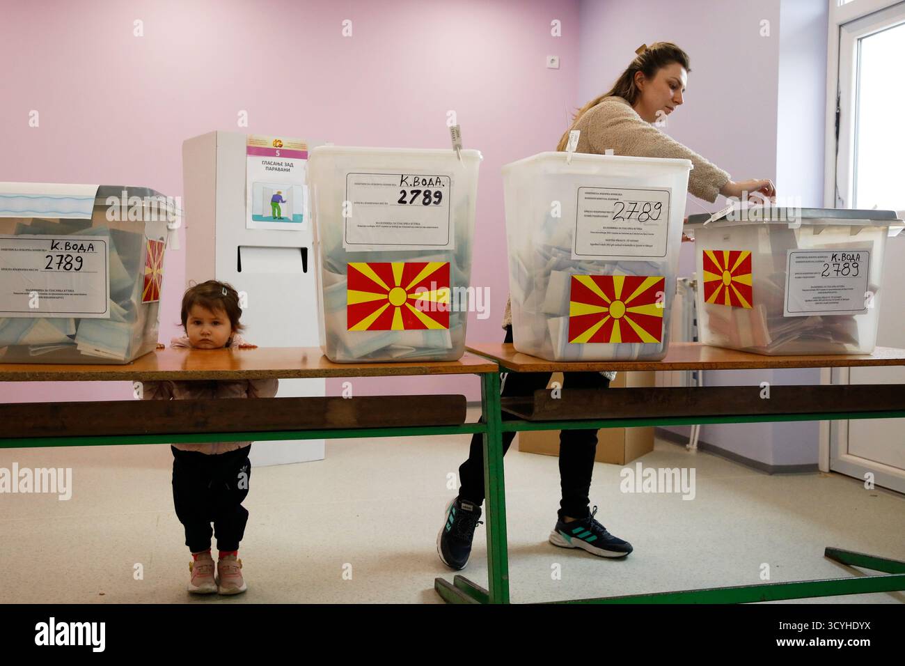 A little girl looks on as a woman casts her ballot for the local ...