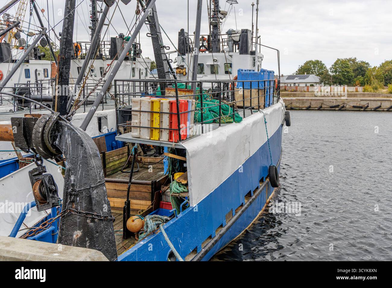 The stern of a blue and white fishing trawler docked in a busy harbor ...