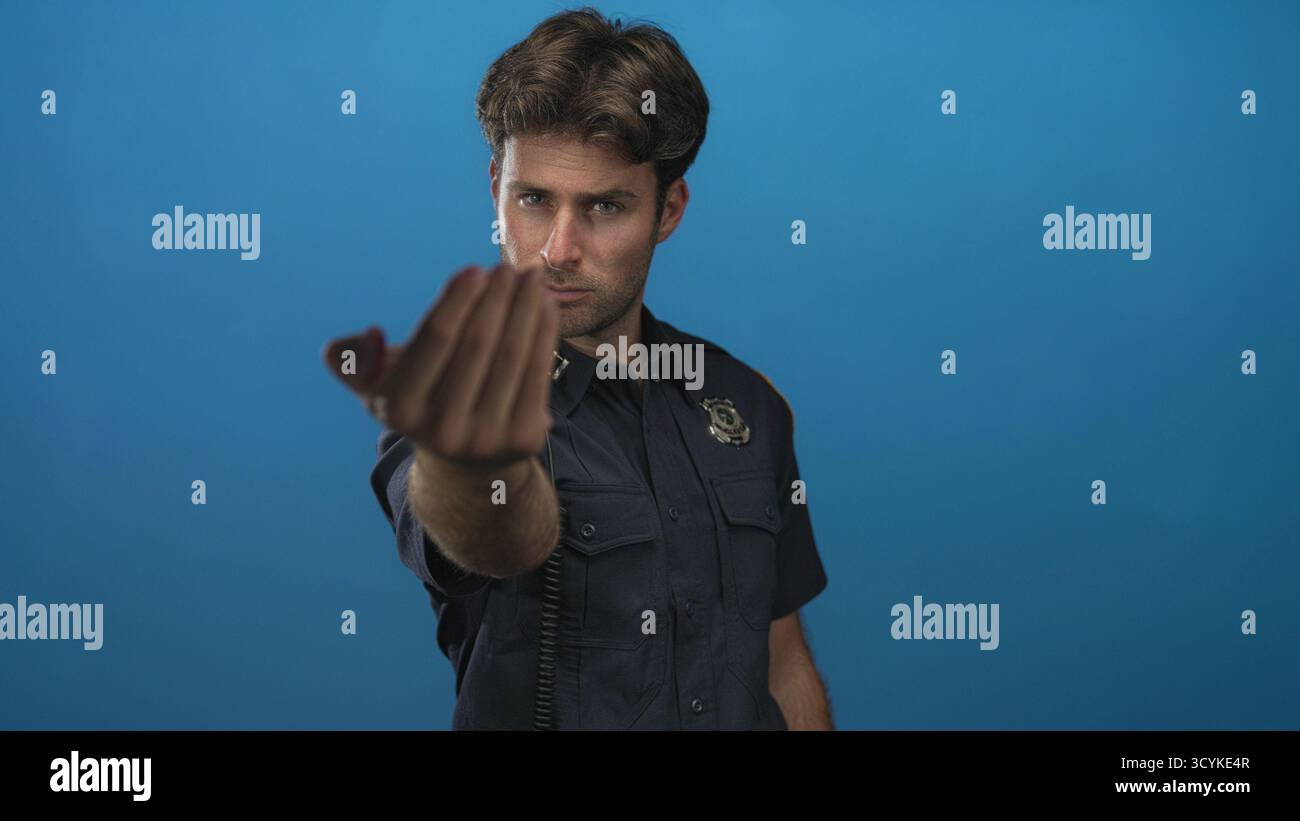 Policeman man pointing finger toward camera in blue studio wearing navy ...