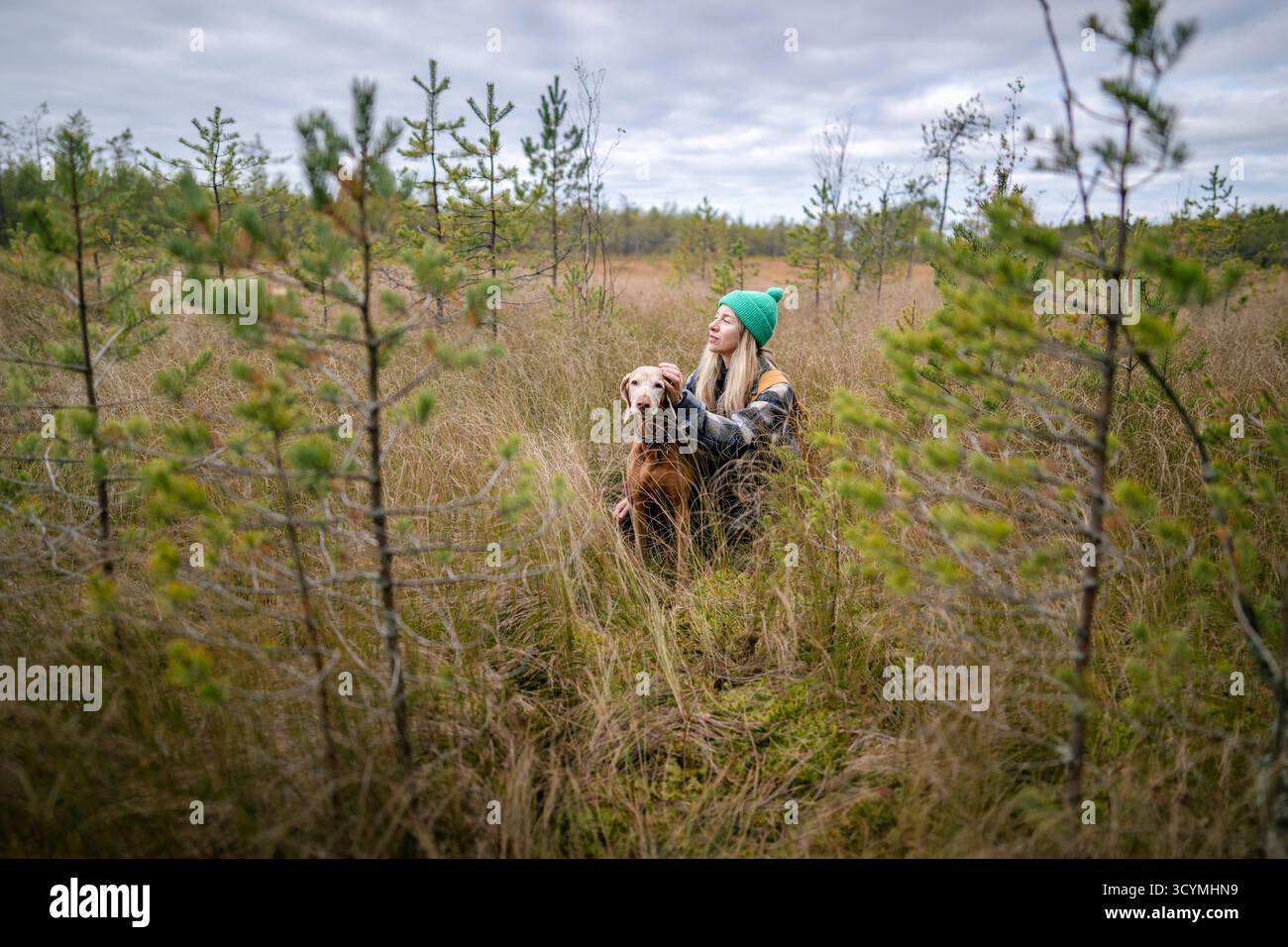 Woman embrace dog, sitting together in dry sedge grass, resting after ...
