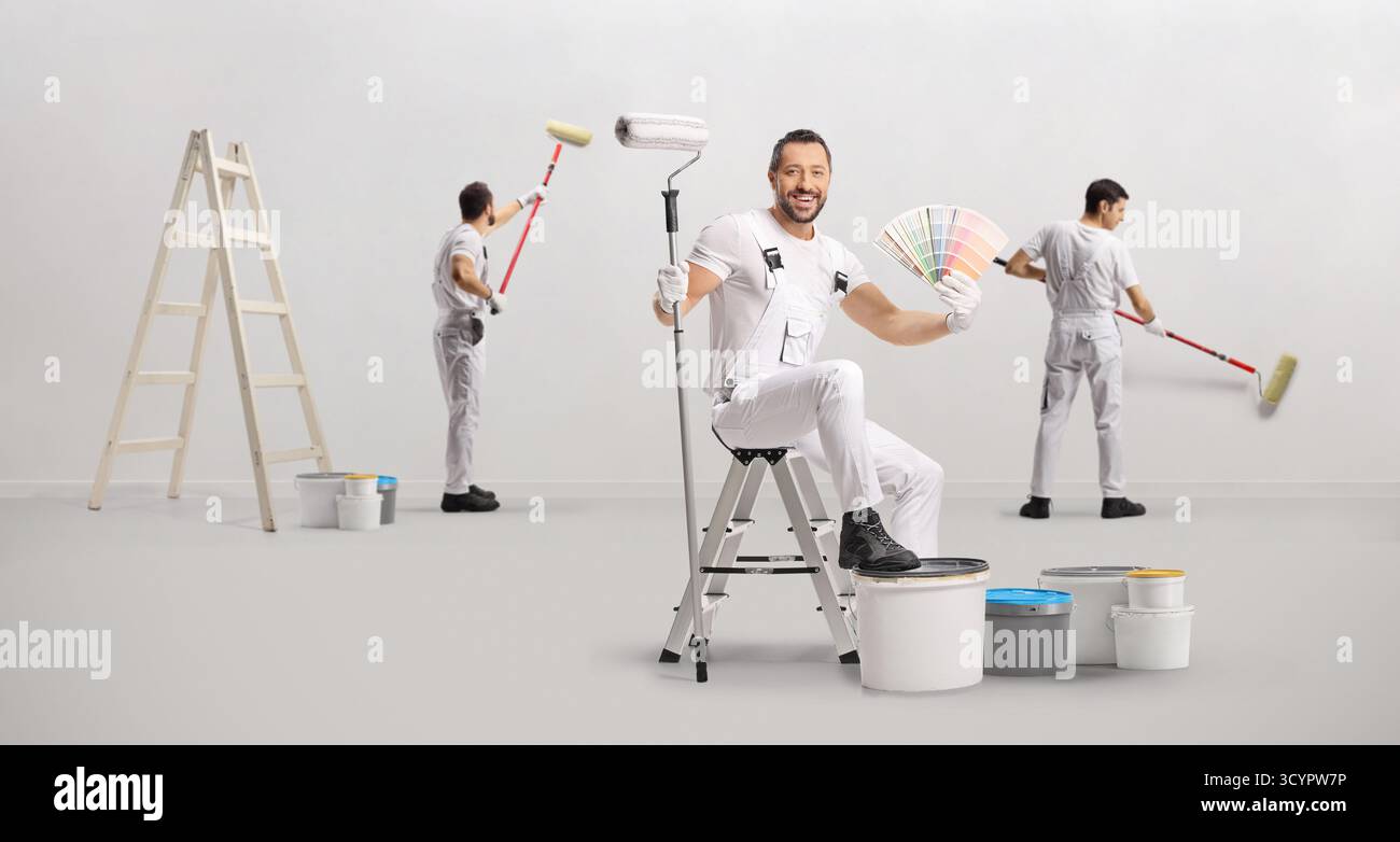Team of painters at work with paint buckets and rollers painting a wall ...