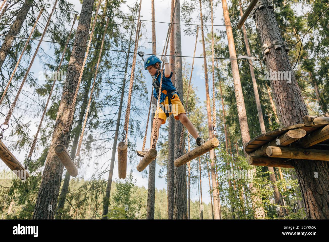 Boy balancing on hanging logs in forest high ropes course Stock Photo ...