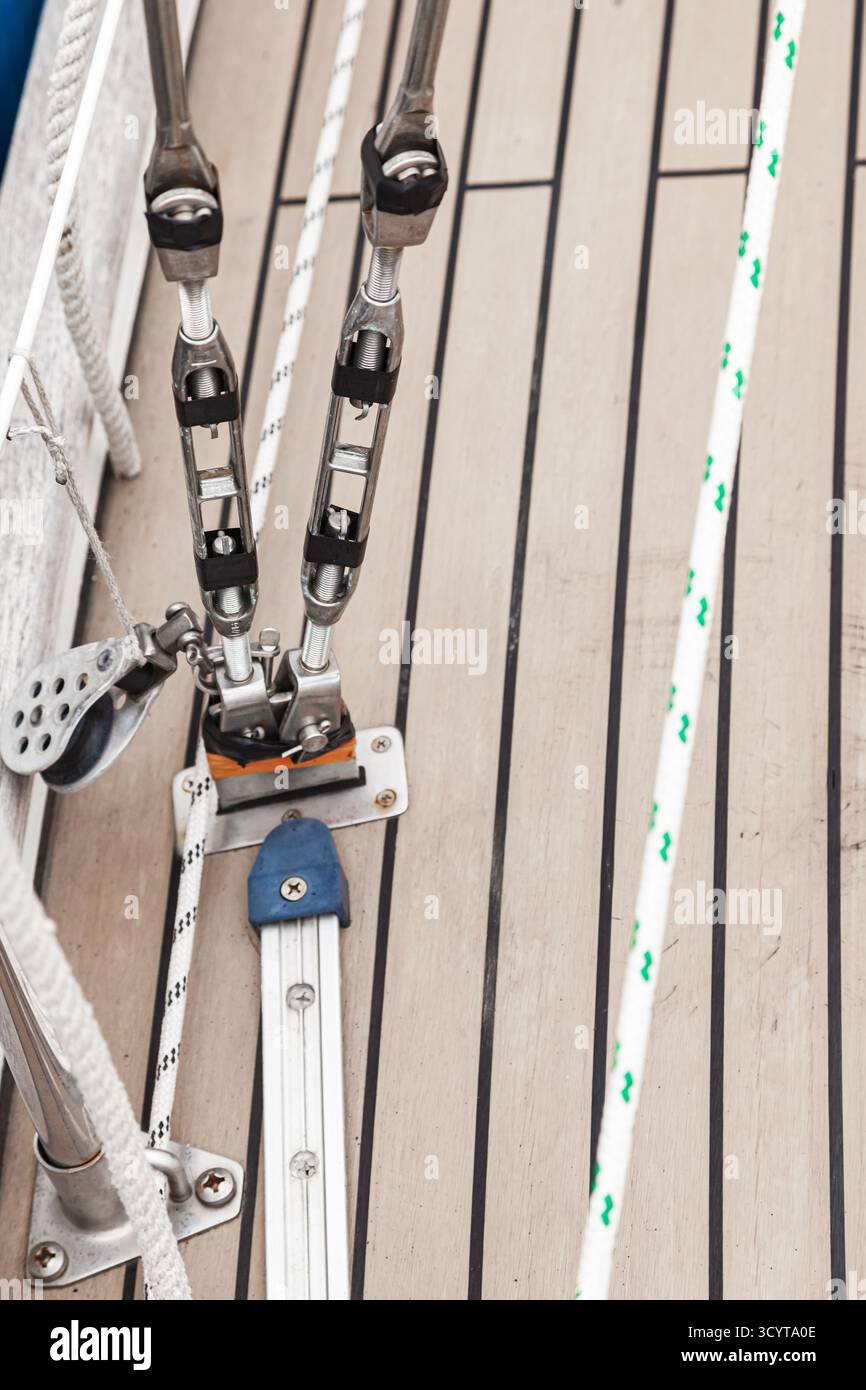 Part of the teak deck of a sailing yacht with stainless steel lanyards and sail ropes stretched ...