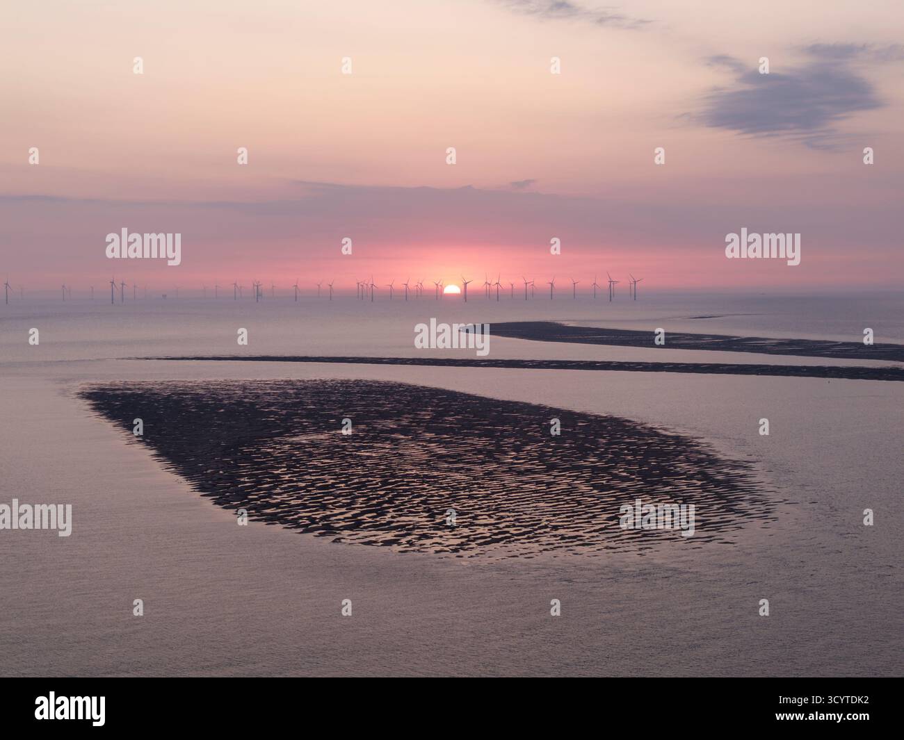 The sun sets behind wind turbines in Liverpool Bay with an isolated ...