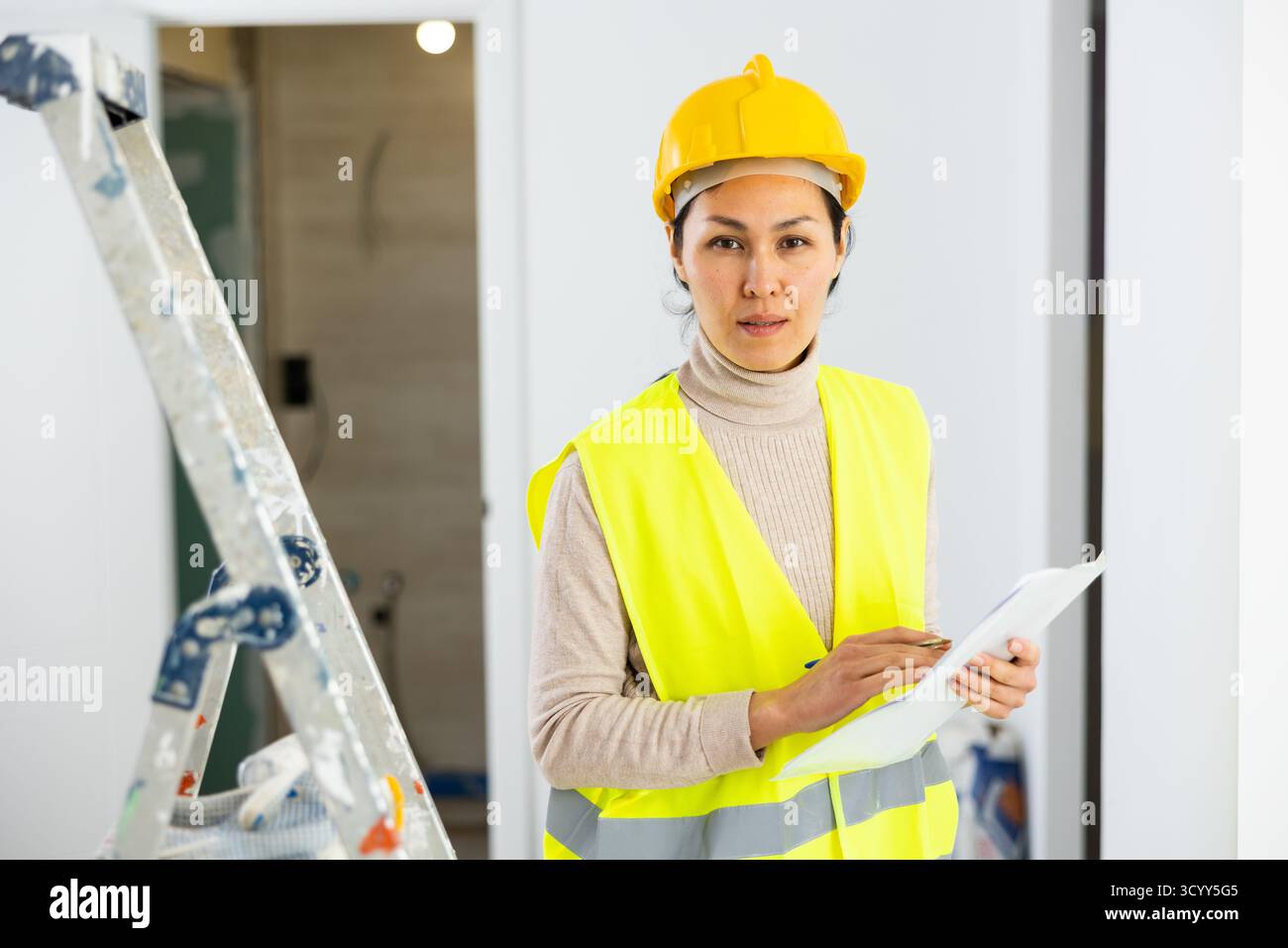 Woman foreman in a protective helmet and yellow vest checks the ...