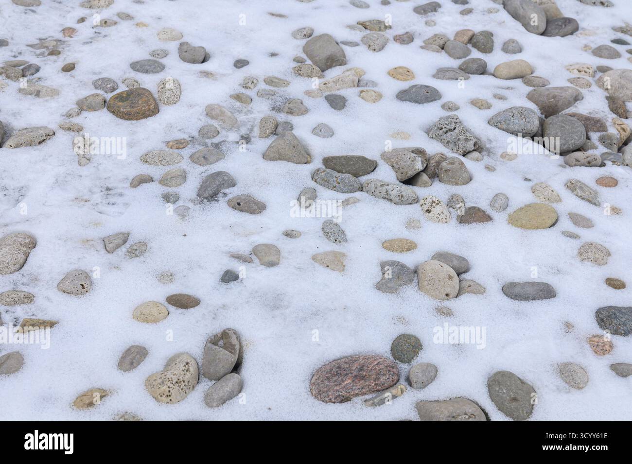 Small and large rocks lie scattered on the snowy ground, partially ...