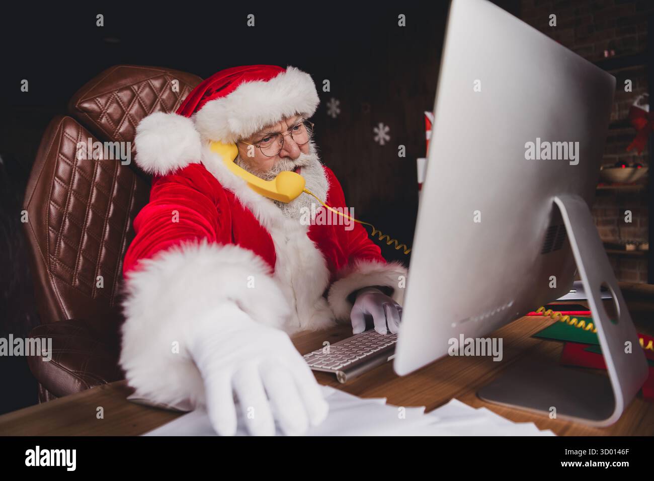 Santa at desk working on computer with yellow phone in a cozy home ...