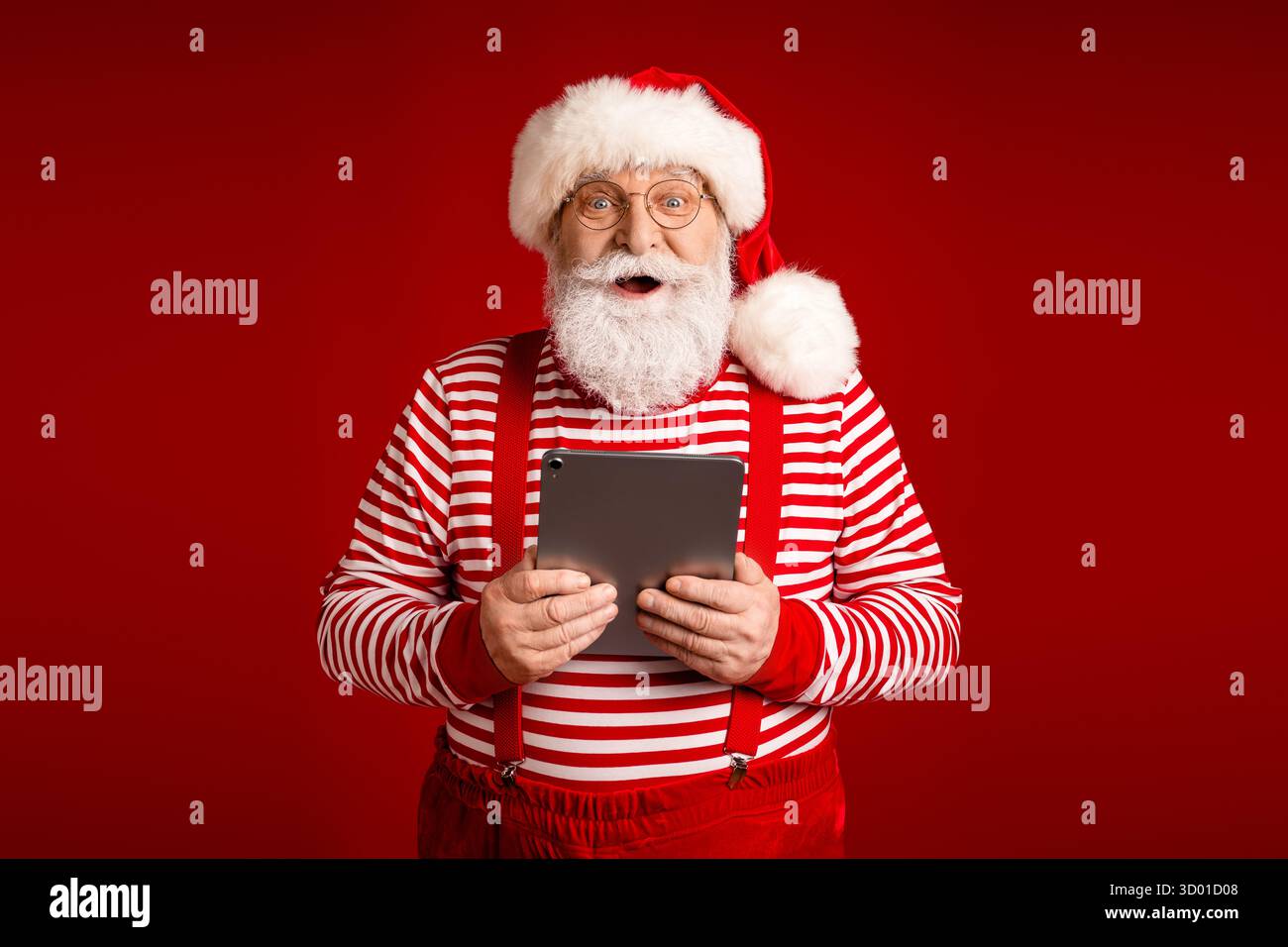 Santa Claus with tablet smiles in a red festive studio wearing striped ...