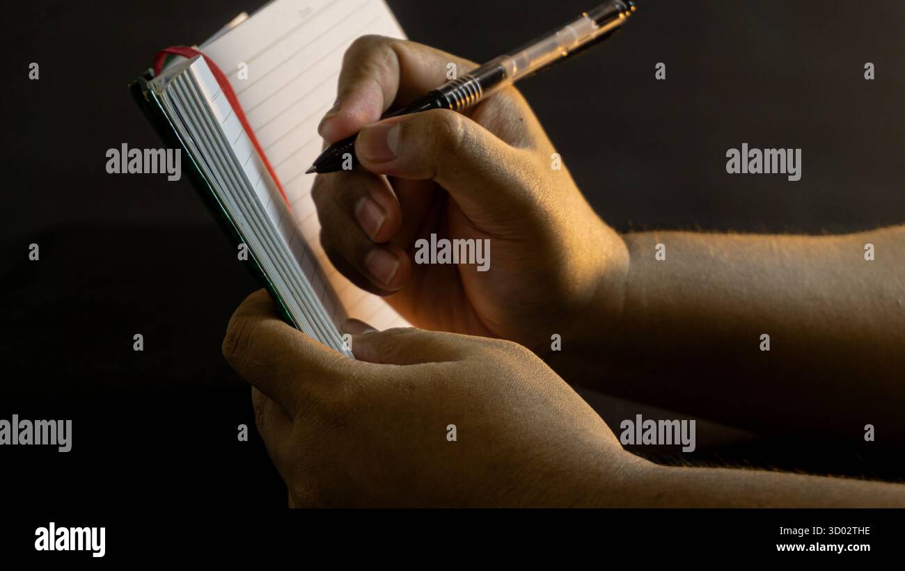 Side view of male hand holding upright notebook and pen under warm ...
