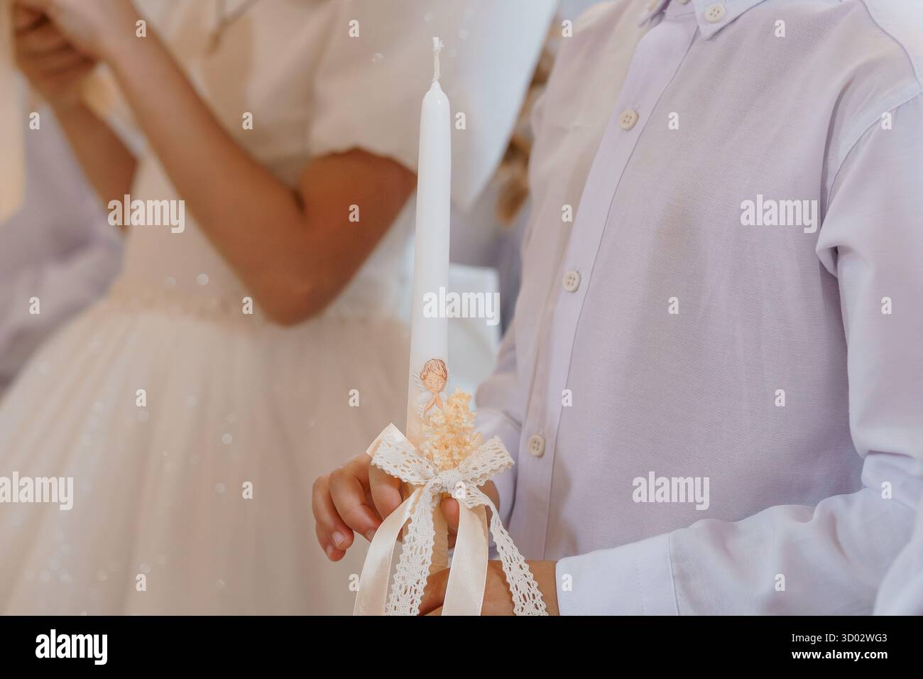 A young boy holds a lit baptism candle adorned with a lace bow during ...