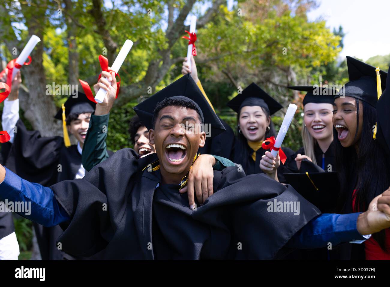 Graduating students holding diplomas, wearing caps and gowns ...