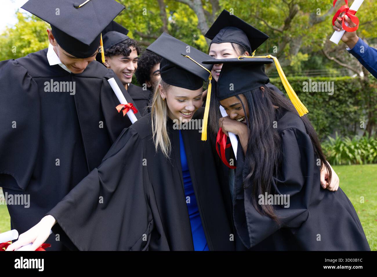 Graduating students in caps and gowns celebrating together outdoors ...