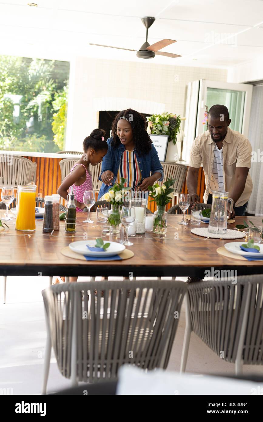 Family setting table together for meal, arranging flowers and placing ...