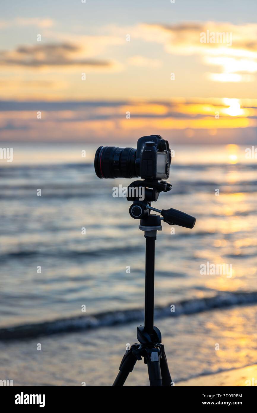 Tripod with camera on sand in golden light by the seaside. Camera and ...
