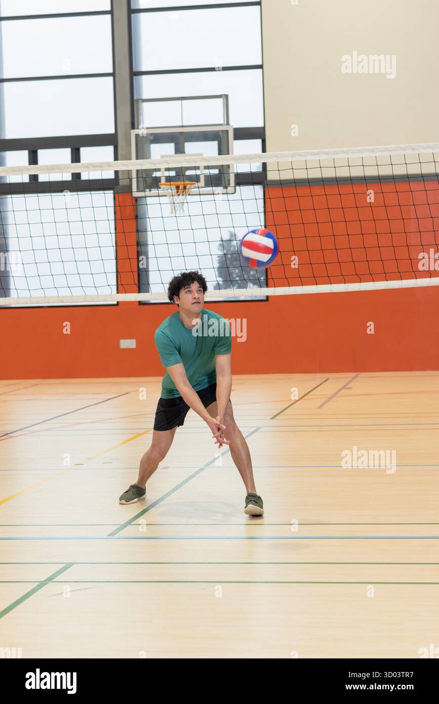 Teenage male volleyball player in shirt passing volleyball in gym under ...