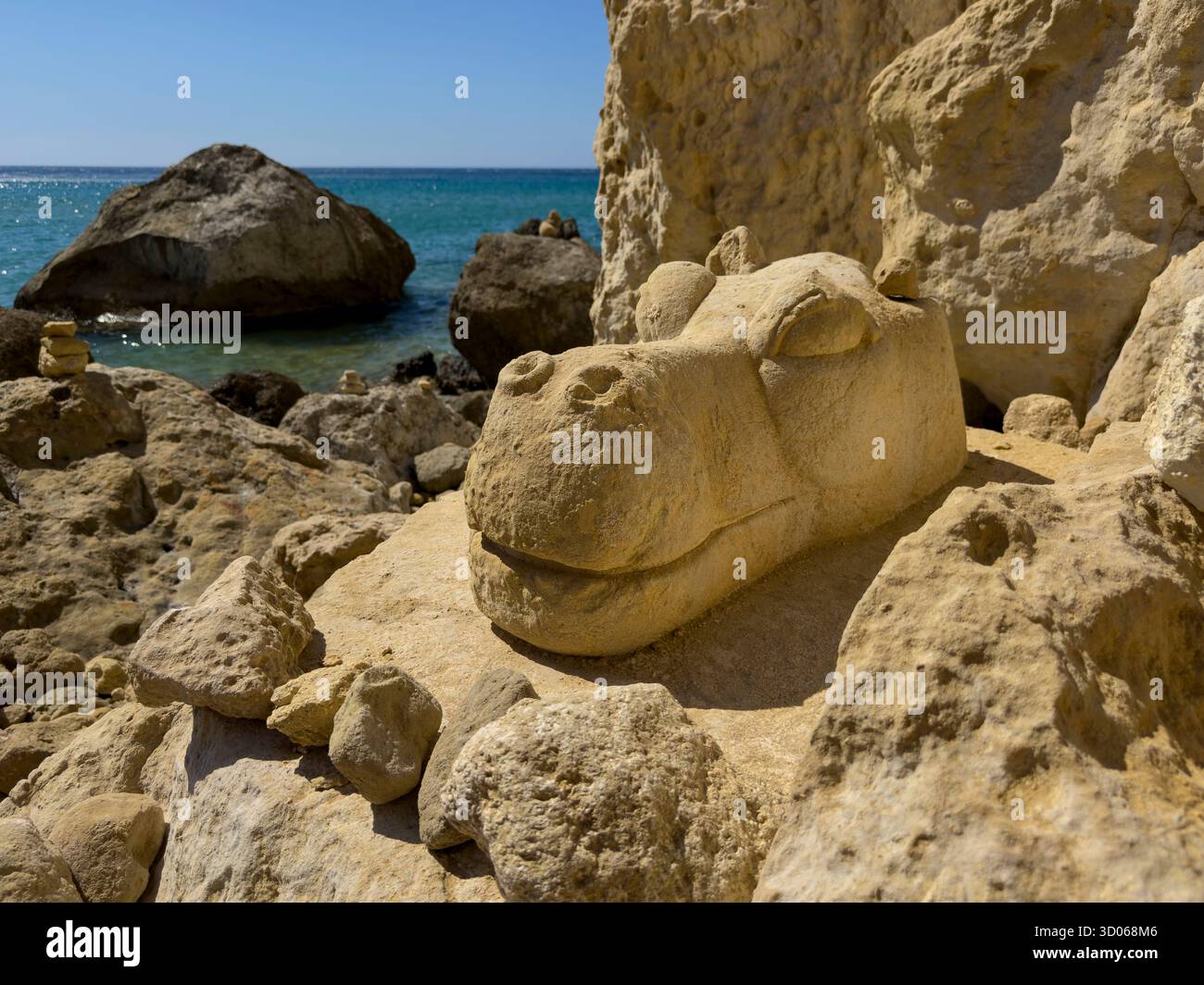 Carving of a hippopatamus in the shoreline rocks of the red sand beach ...