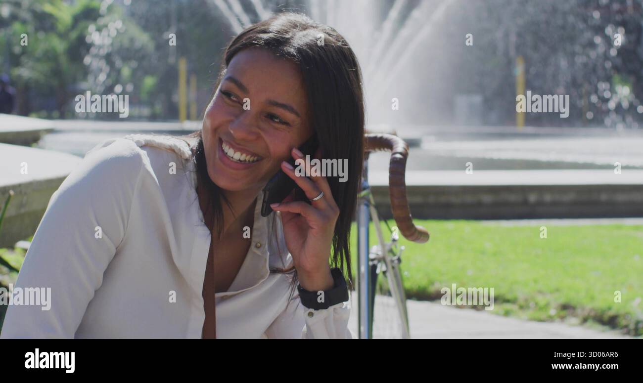 Woman wearing smartwatch talking on smartphone on park bench, with drop ...