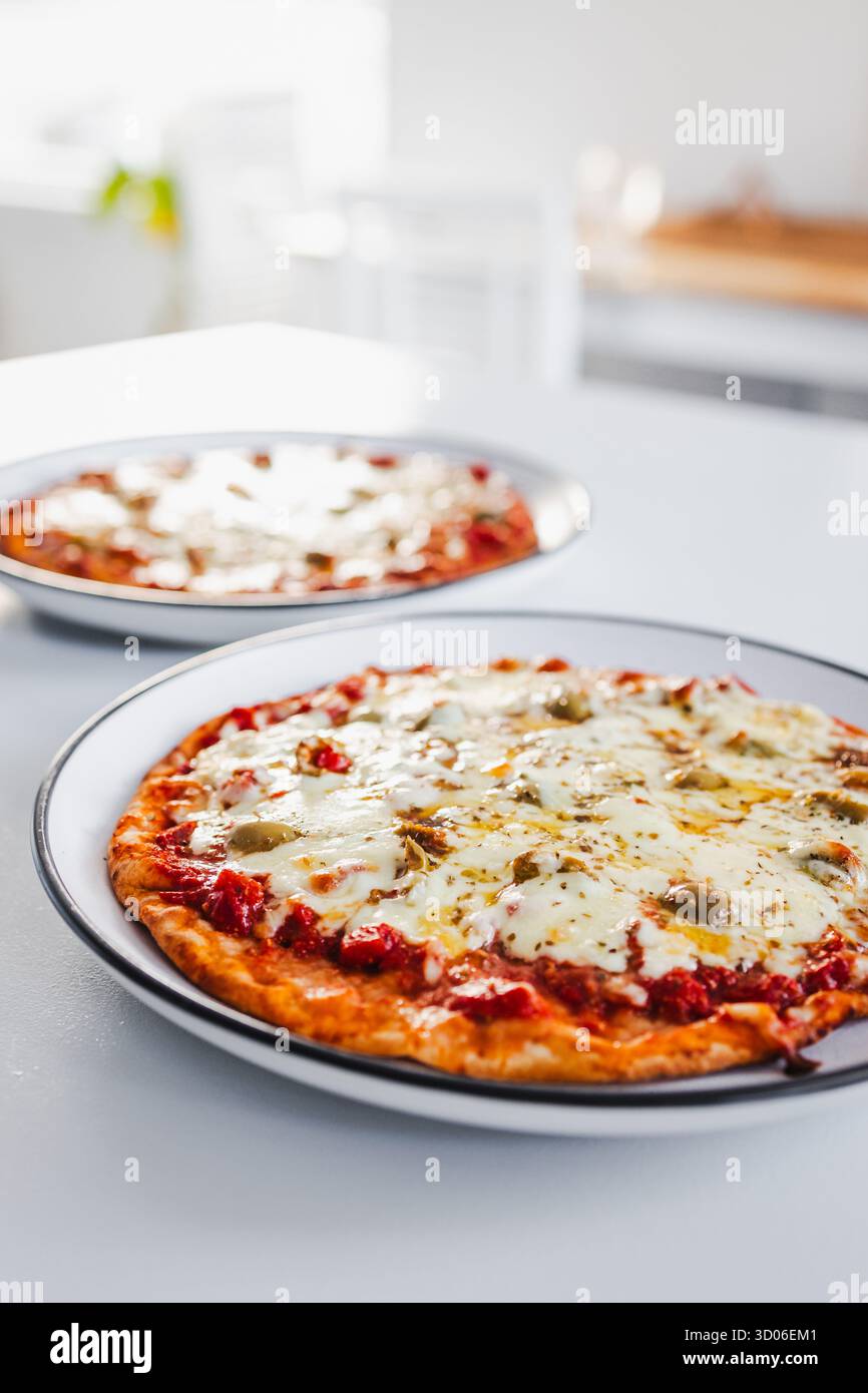 two small margherita pizzas with olives on large plates, symbolizing ...